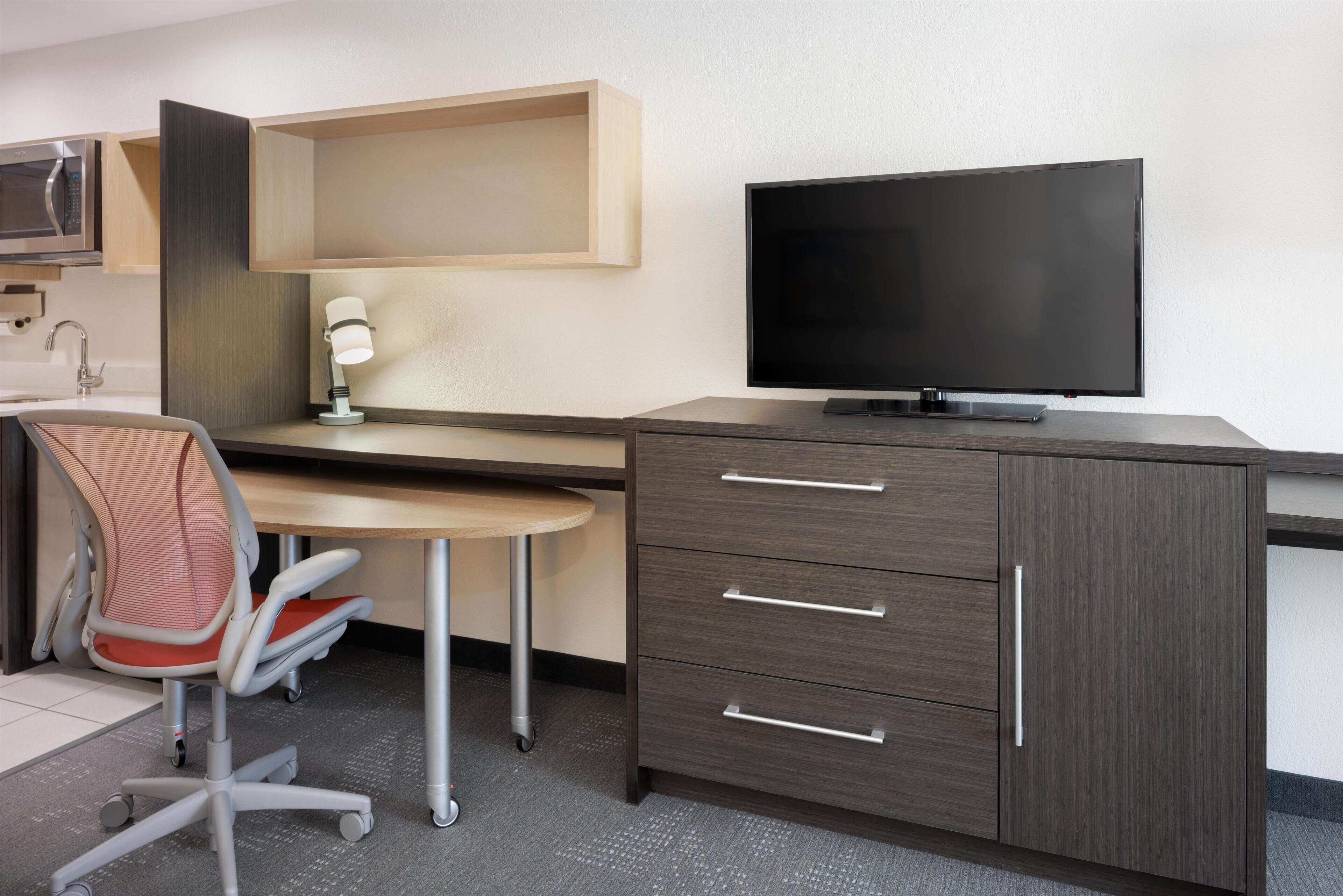 Quarto de hotel moderno com uma escrivaninha, televisão de tela plana, uma cadeira e um armário.