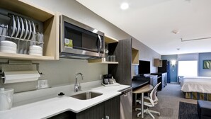 Quarto de hotel compacto com cozinha compacta, uma cama, uma escrivaninha e uma cadeira.