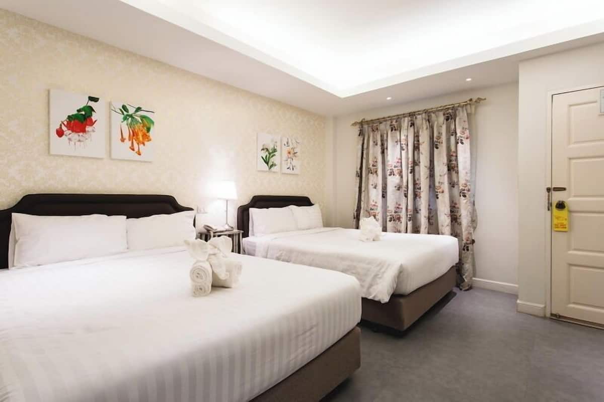 Quarto de hotel com duas camas, uma mesa de cabeceira, uma luminária e cortinas florais.