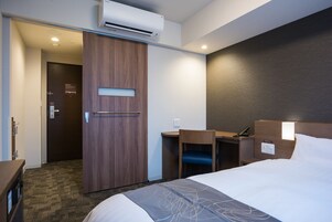 Quarto de hotel com cama, escrivaninha, cadeira e ar condicionado.