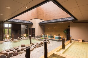 Uma onsen japonesa tradicional com duas piscinas termais, bancos de madeira e um caminho de pedra.