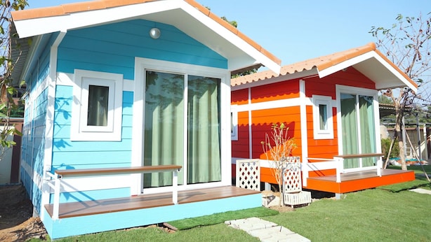Duas pequenas casas térreas com varanda, uma pintada de azul e outra de vermelho, ambas com detalhes em branco e telhado de telhas.