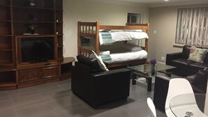 Uma sala de estar com televisão, sofá, mesa de centro, beliche e estante de livros.