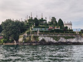 Um jardim paisagístico com estátuas e um edifício circular, cercado por água.
