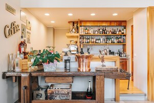 Uma área de bar com prateleiras de garrafas de bebidas, uma torneira de cobre e um balcão de madeira com objetos decorativos.