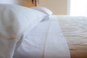 Um close-up de uma cama com roupa de cama branca e um cobertor bege.