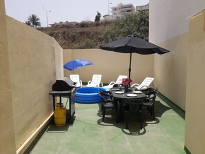 Um pátio com mesa, cadeiras, churrasqueira e piscina inflável.