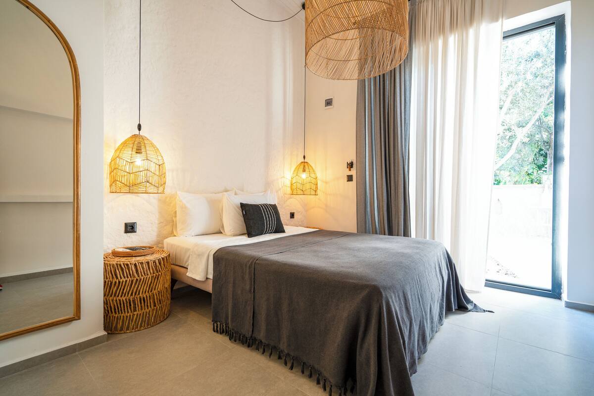 Quarto com cama, luminárias de cabeceira, espelho e janela com cortinas.