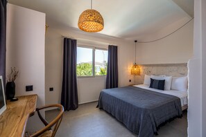 Quarto com cama, mesa de cabeceira e janela com cortinas.