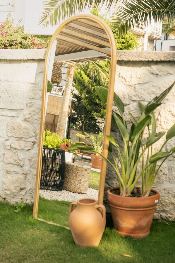 Um jardim com um espelho refletindo um espaço de pátio, plantas em vasos e uma parede de pedra.