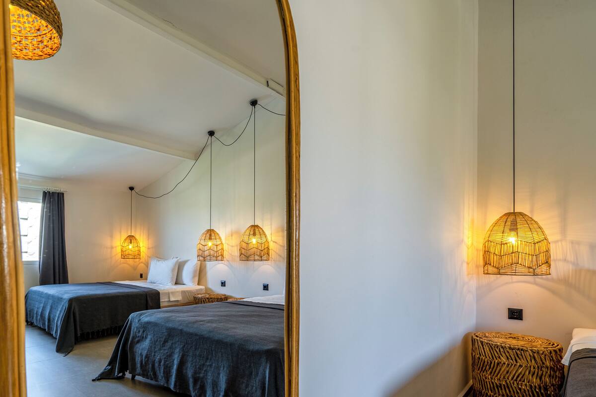 Quarto de hotel com duas camas, um espelho grande e três luminárias fixadas na parede.