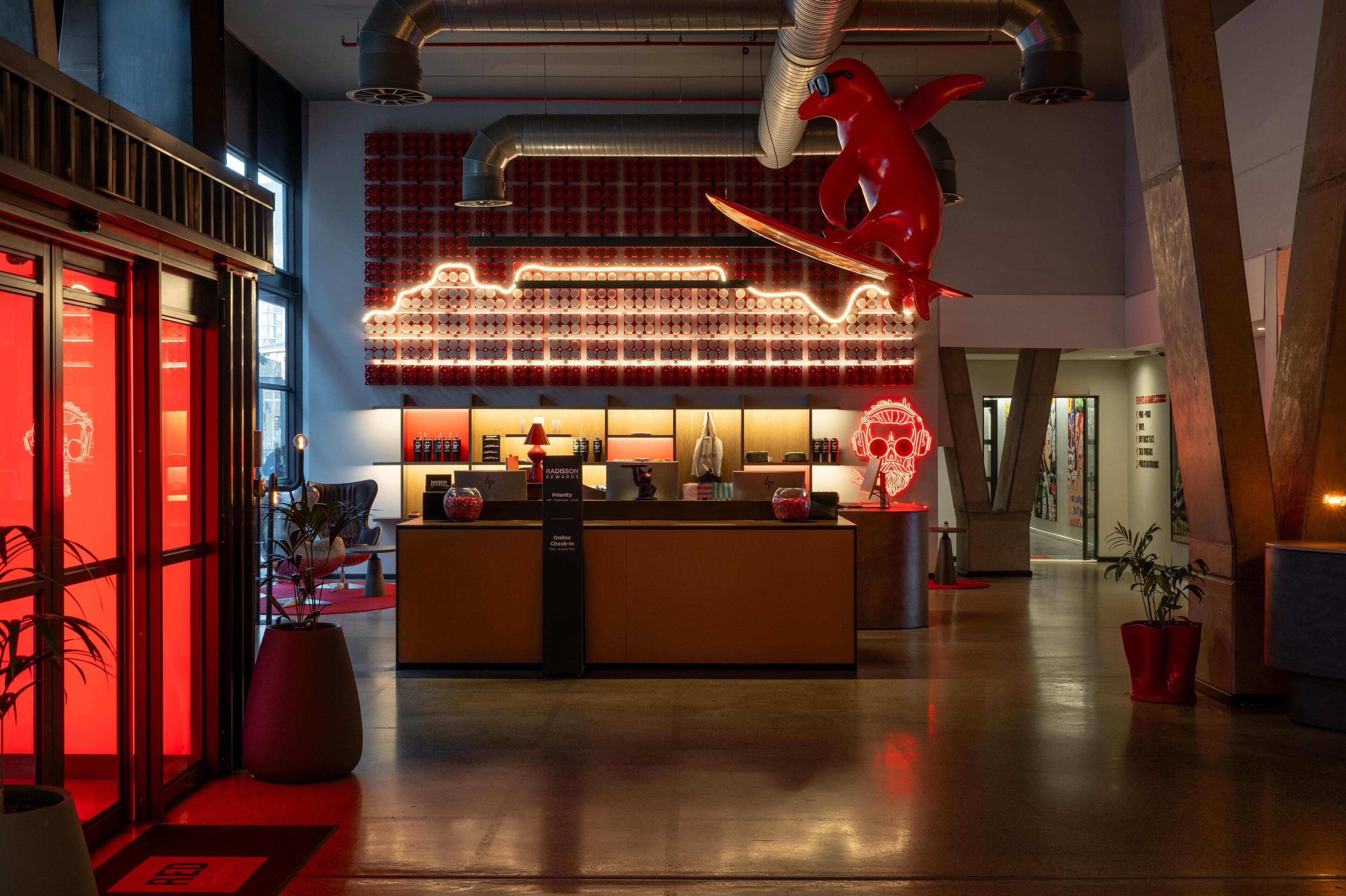 Uma área de recepção moderna com uma parede iluminada em vermelho, uma escultura vermelha grande e um balcão de recepção com computadores.