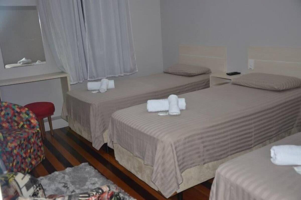 Quarto de hotel com duas camas, uma escrivaninha pequena, uma cadeira e um espelho.