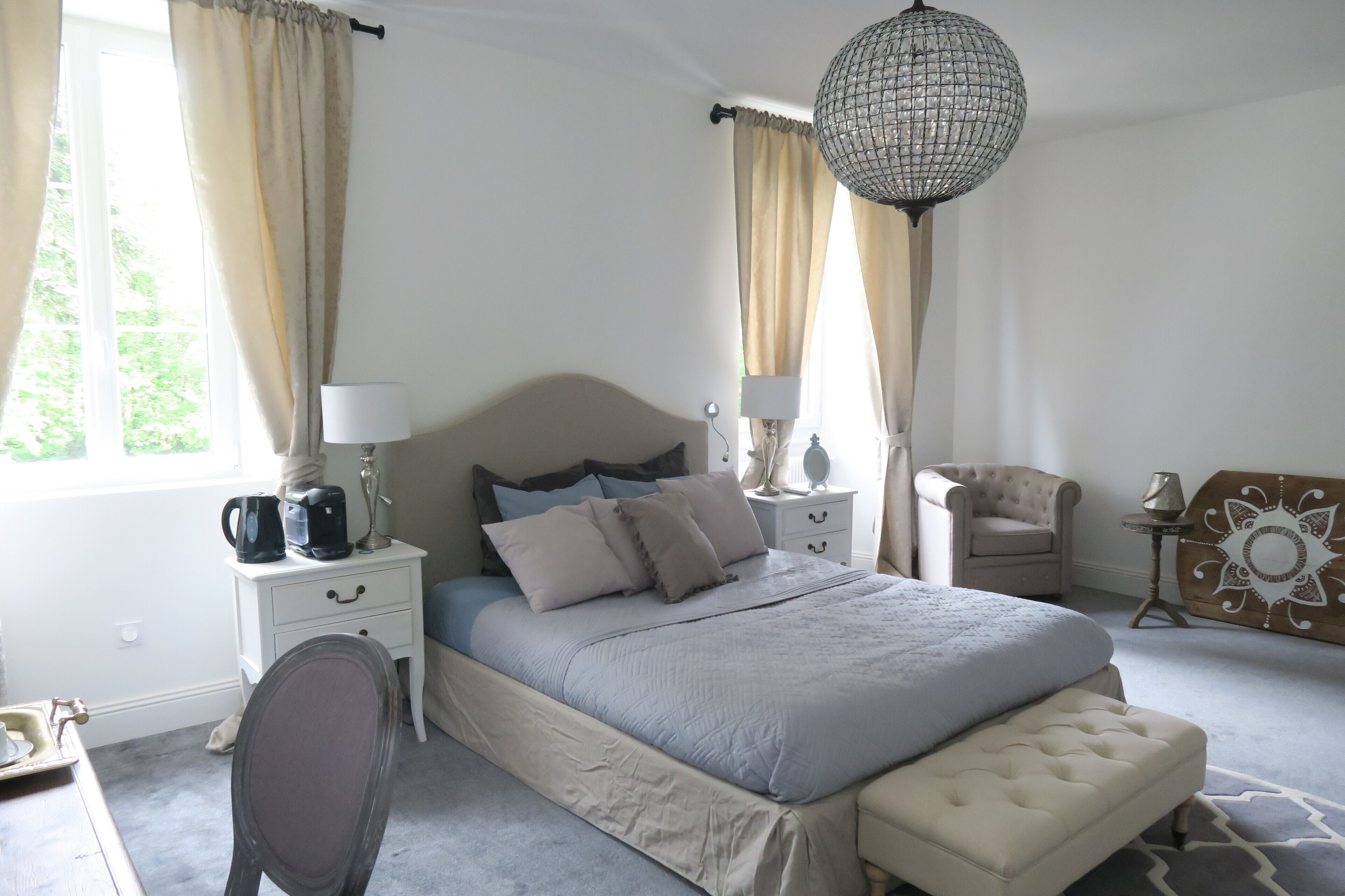 Quarto com cama, mesas de cabeceira, uma cadeira, luminária e um objeto decorativo na parede.