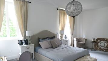 Quarto com cama, mesas de cabeceira, uma cadeira, luminária e um objeto decorativo na parede.