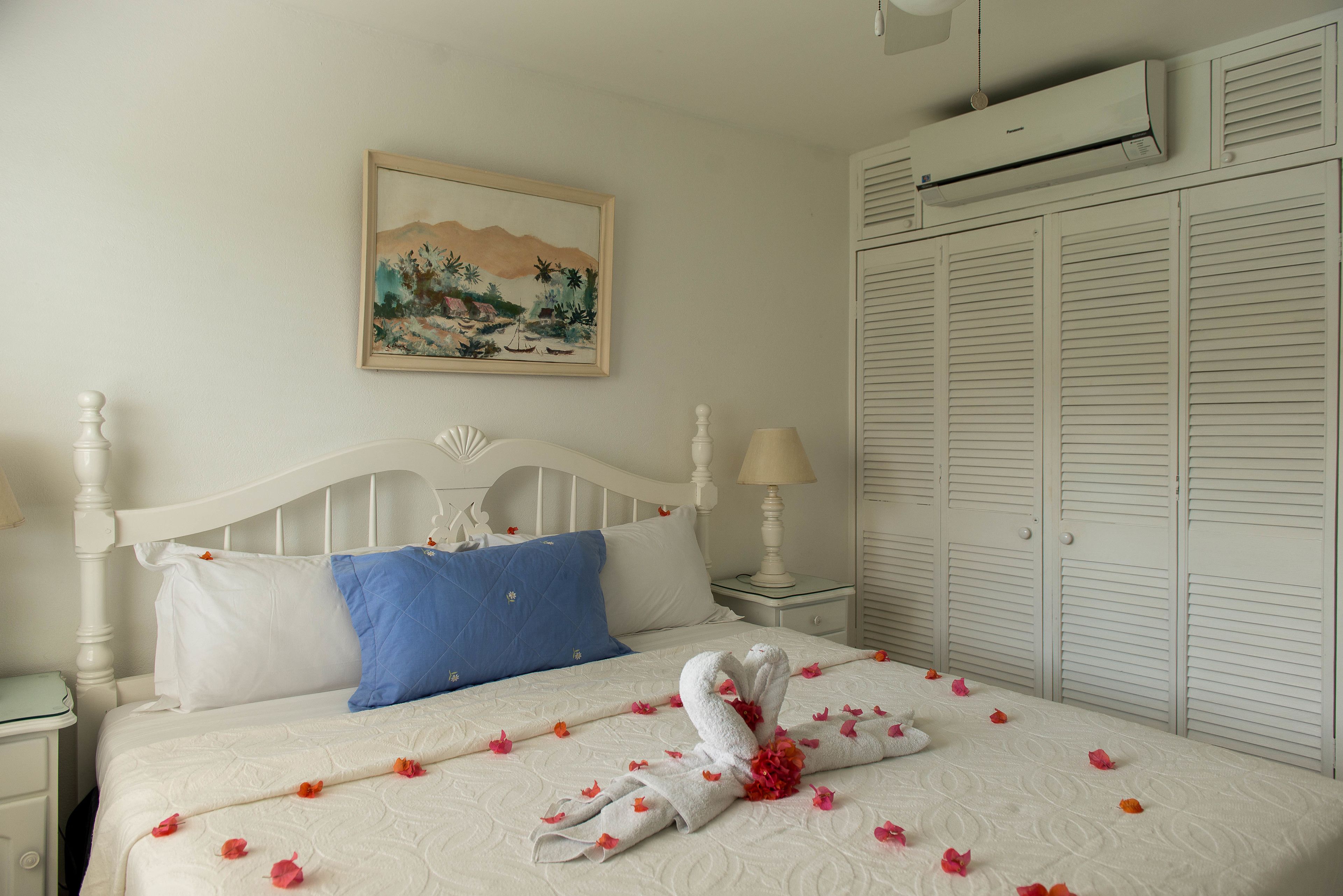 Cama bem arrumada com arte de toalha, um quadro na parede e ar condicionado branco acima da cama.