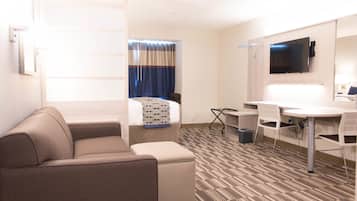 Quarto de hotel com sofá, cama, escrivaninha, cadeiras, televisão e tapete estampado.