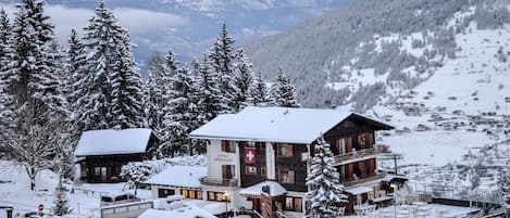 Um hotel com restaurante, rodeado por árvores e montanhas cobertas de neve.