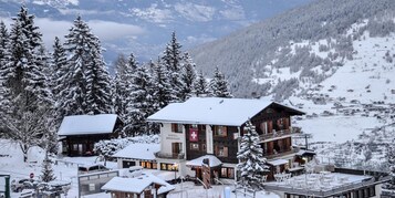 Um hotel com restaurante, rodeado por árvores e montanhas cobertas de neve.