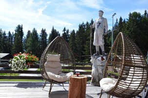Uma estátua de um homem segurando um bastão, cercada por cadeiras de vime e uma mesa de madeira em um deck de madeira.