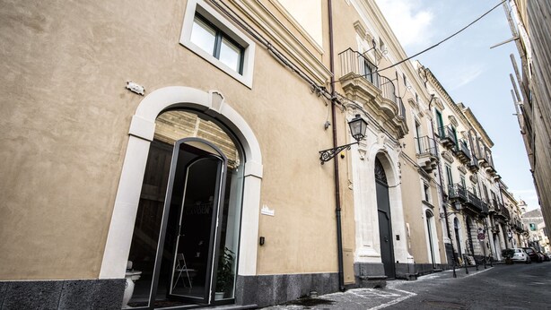 Um edifício com uma grande entrada em arco, uma pequena varanda e uma rua com carros estacionados.