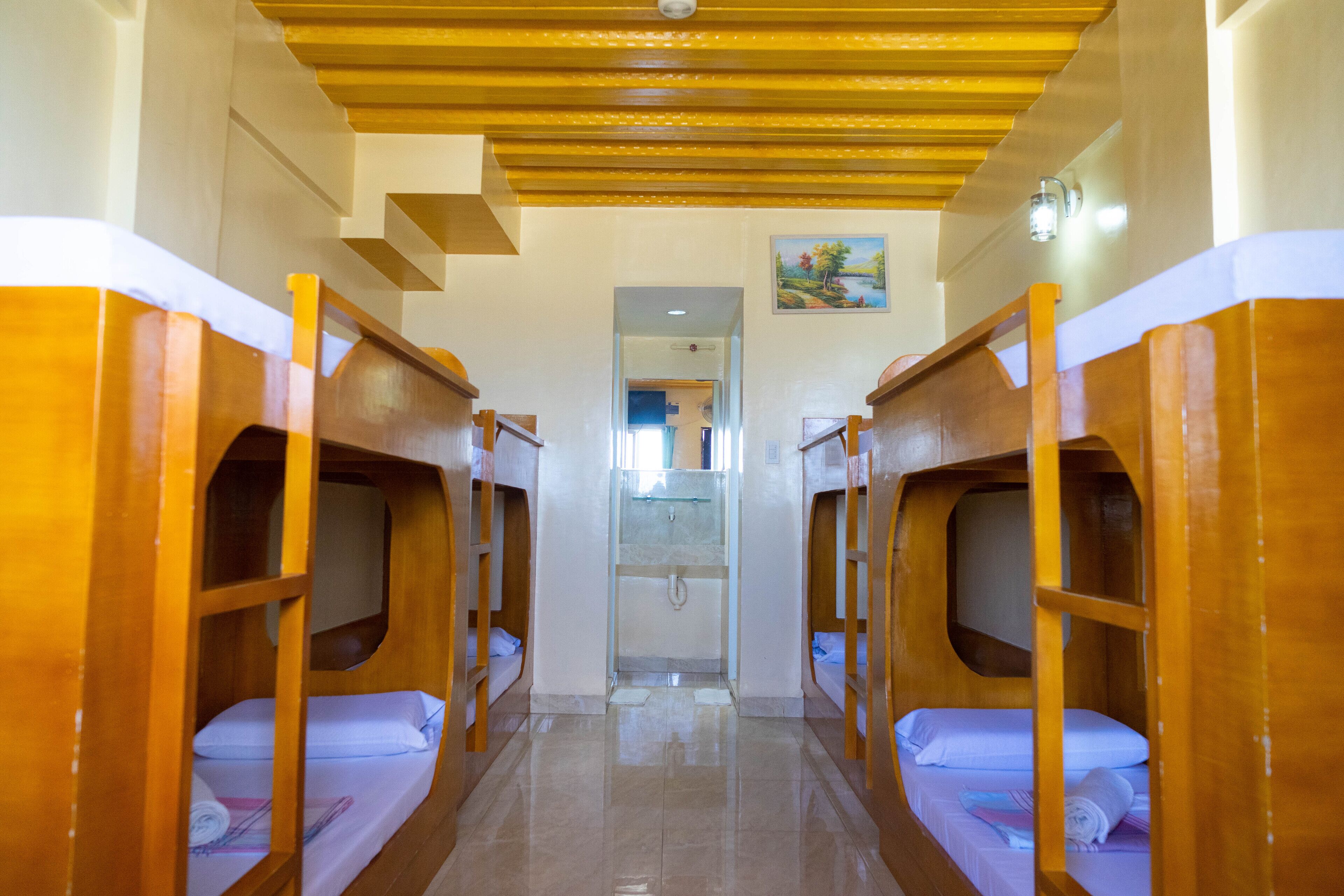 Um corredor com beliches, área de chuveiro e um quadro na parede.