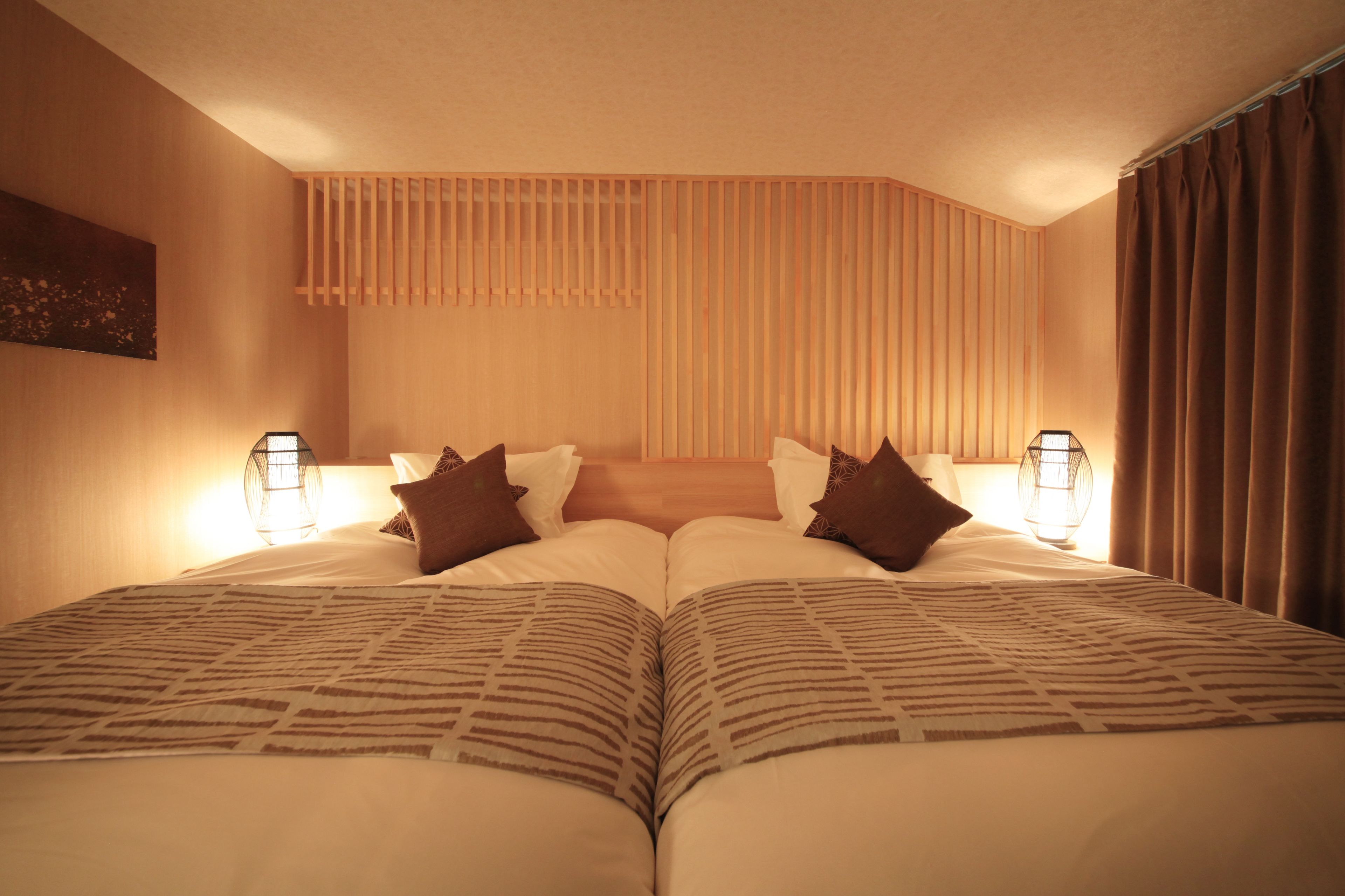 Uma cama de casal com colcha estampada, duas luminárias de cabeceira e cabeceira com ripas verticais.