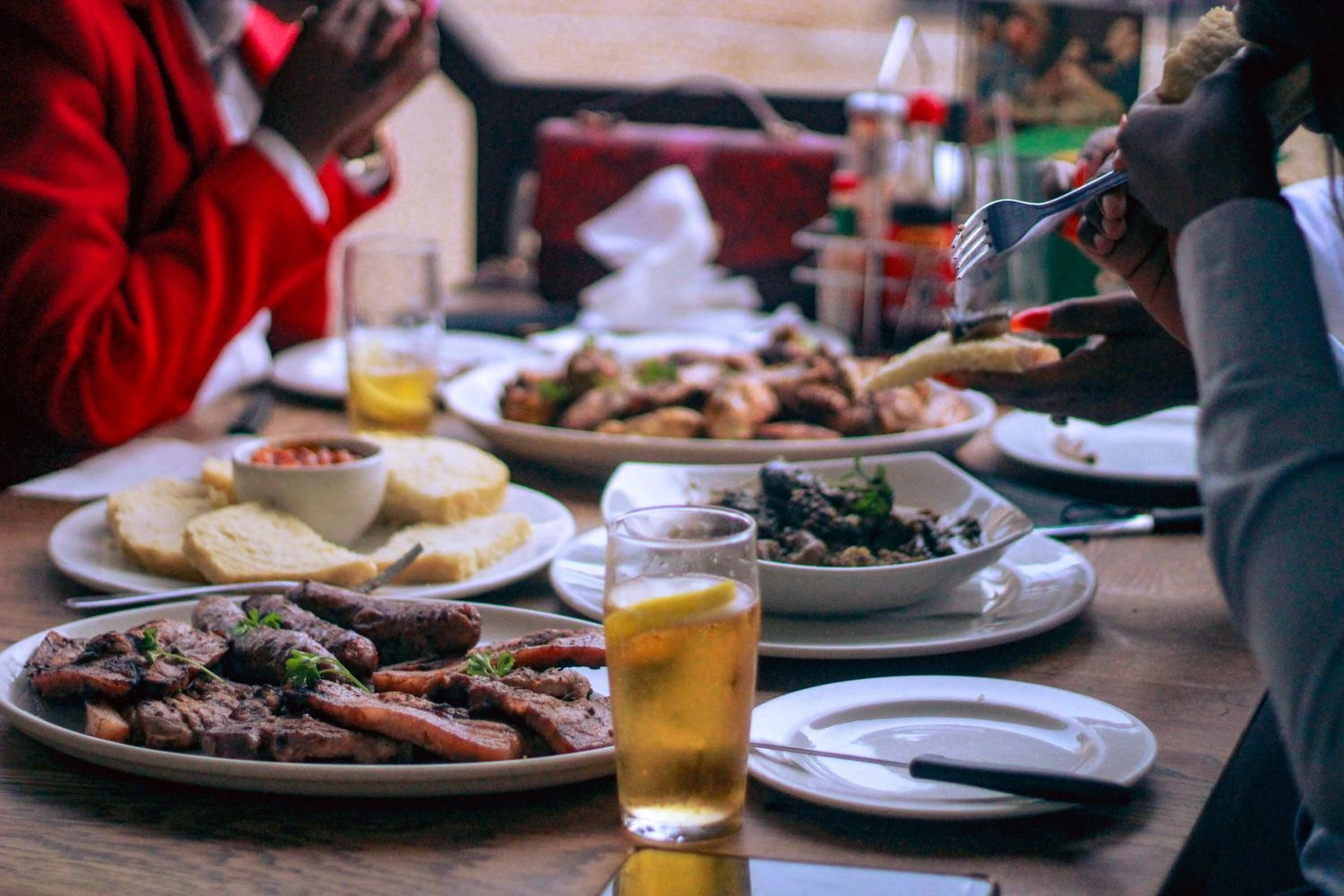 Uma mesa de jantar com diversos pratos, incluindo carne, pão e um copo de cerveja.