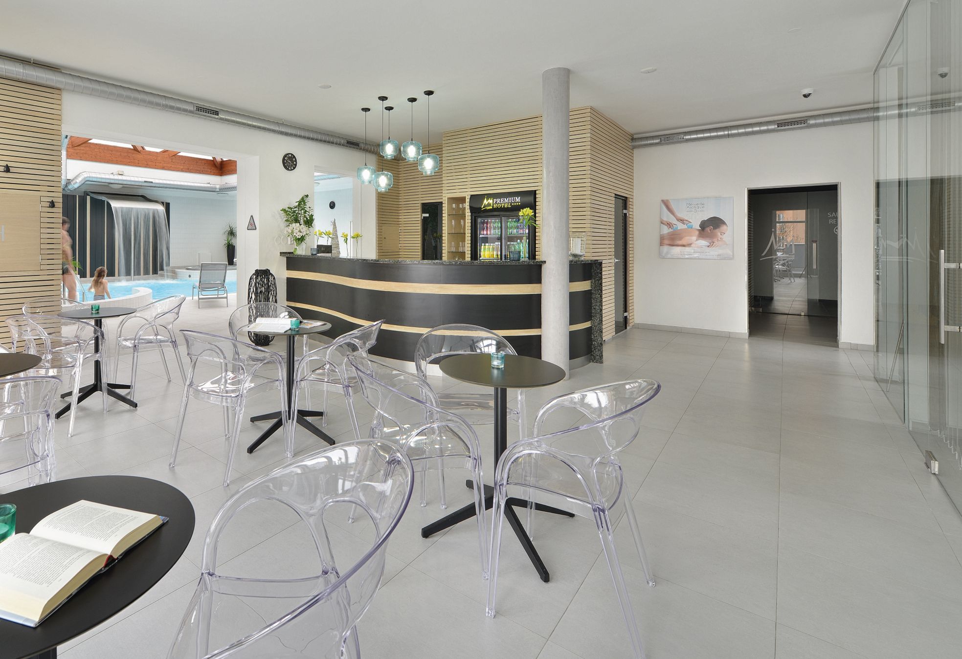Uma área interna de piscina moderna com cadeiras e mesas de plástico transparente, um bar com a placa 'Premium Poolside' e uma parede de vidro com vista para a piscina.
