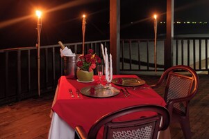 Mesa posta para dois em deck de madeira, com toalha vermelha, velas, garrafa de champanhe e bolo verde decorado com rosas vermelhas.