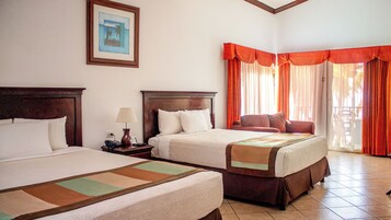 Quarto de hotel com duas camas, uma mesa de cabeceira com abajur, uma cadeira e uma janela com cortinas.
