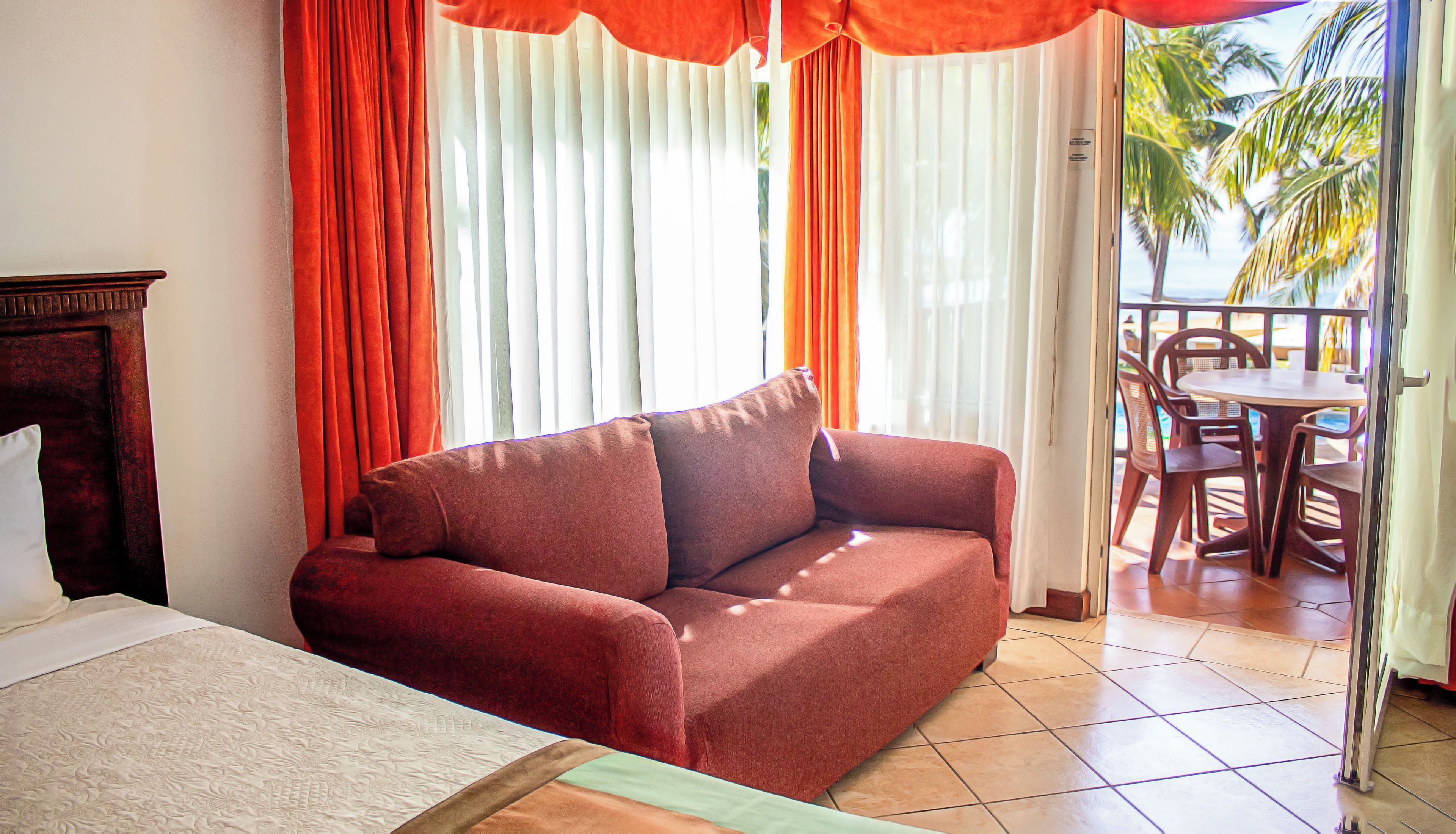Quarto com sofá, cama e vista para o exterior através de uma janela com cortinas.
