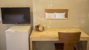 Quarto com televisão de tela plana na parede, escrivaninha de madeira com cadeira e um quadro com almofadas na parede.