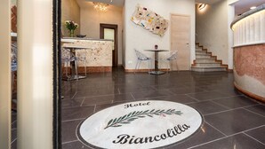 Um saguão de hotel com balcão de atendimento, área de refeições e escadaria.