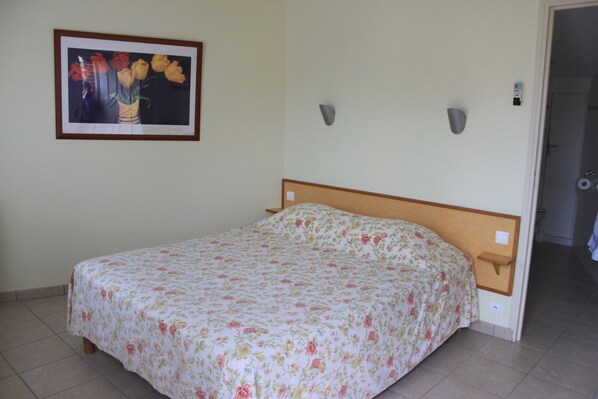 Quarto com colcha floral, cabeceira de madeira, mesa de cabeceira e um quadro na parede.