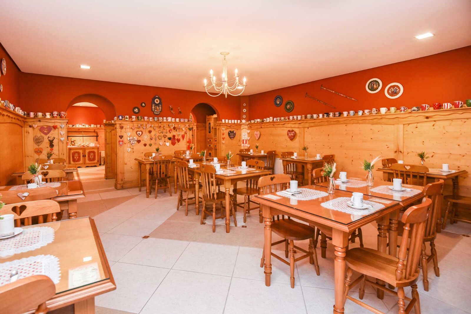 Um restaurante acolhedor com mesas e cadeiras de madeira, um candelabro e decorações em formato de coração nas paredes.