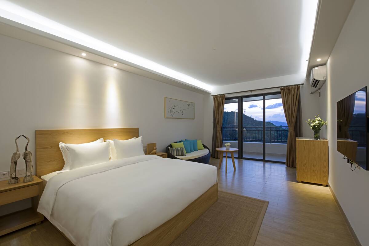 Quarto de hotel moderno com uma cama grande, um sofá pequeno, uma varanda com vista e uma TV.