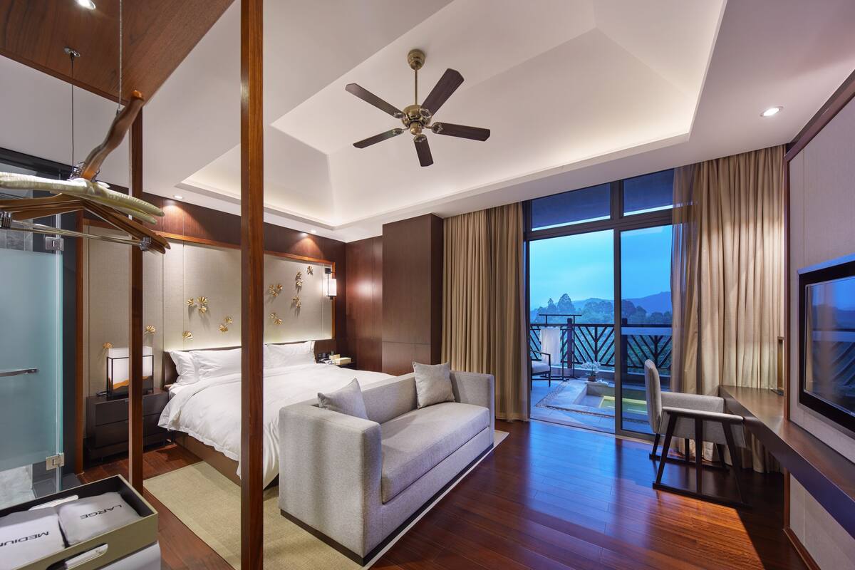 Quarto de hotel moderno com uma cama grande, um sofá, uma escrivaninha e uma varanda com vista.