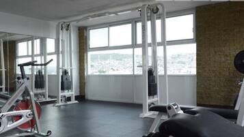 Uma academia com equipamentos de ginástica, grandes janelas e vista para a paisagem urbana.
