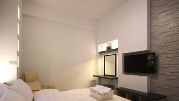Quarto de hotel com cama, cadeira, TV fixada na parede e parede com textura de pedra.