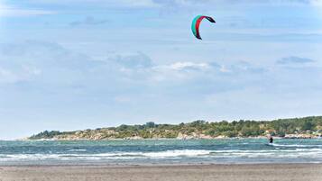 Uma praia com uma pessoa praticando windsurf e uma pipa no céu.