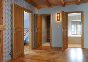 Um corredor com portas de madeira que dão acesso a diversos quartos, uma escadaria e uma janela com vitrais.