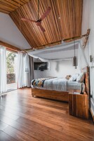 Quarto com teto de madeira, cama com dossel, televisão e mesa de cabeceira.