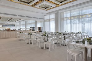 Uma sala de jantar ampla, com cadeiras e mesas brancas, janelas grandes e um design de teto moderno.
