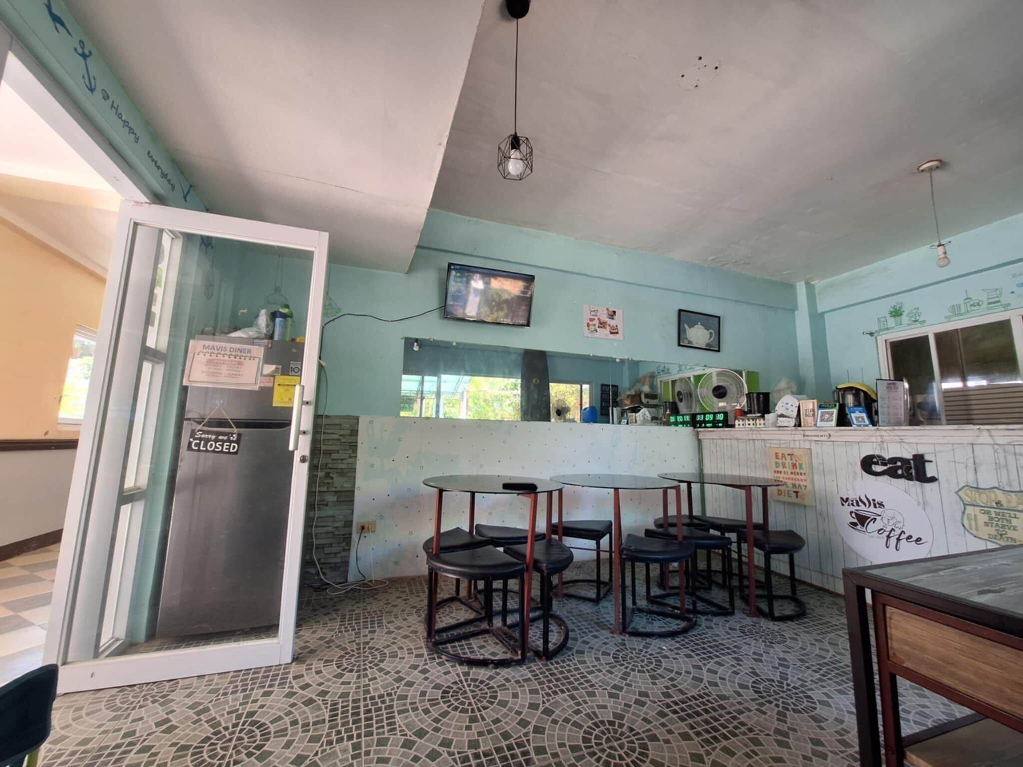 Uma lanchonete fechada com chão de azulejos, um balcão com uma máquina de café e uma televisão na parede.