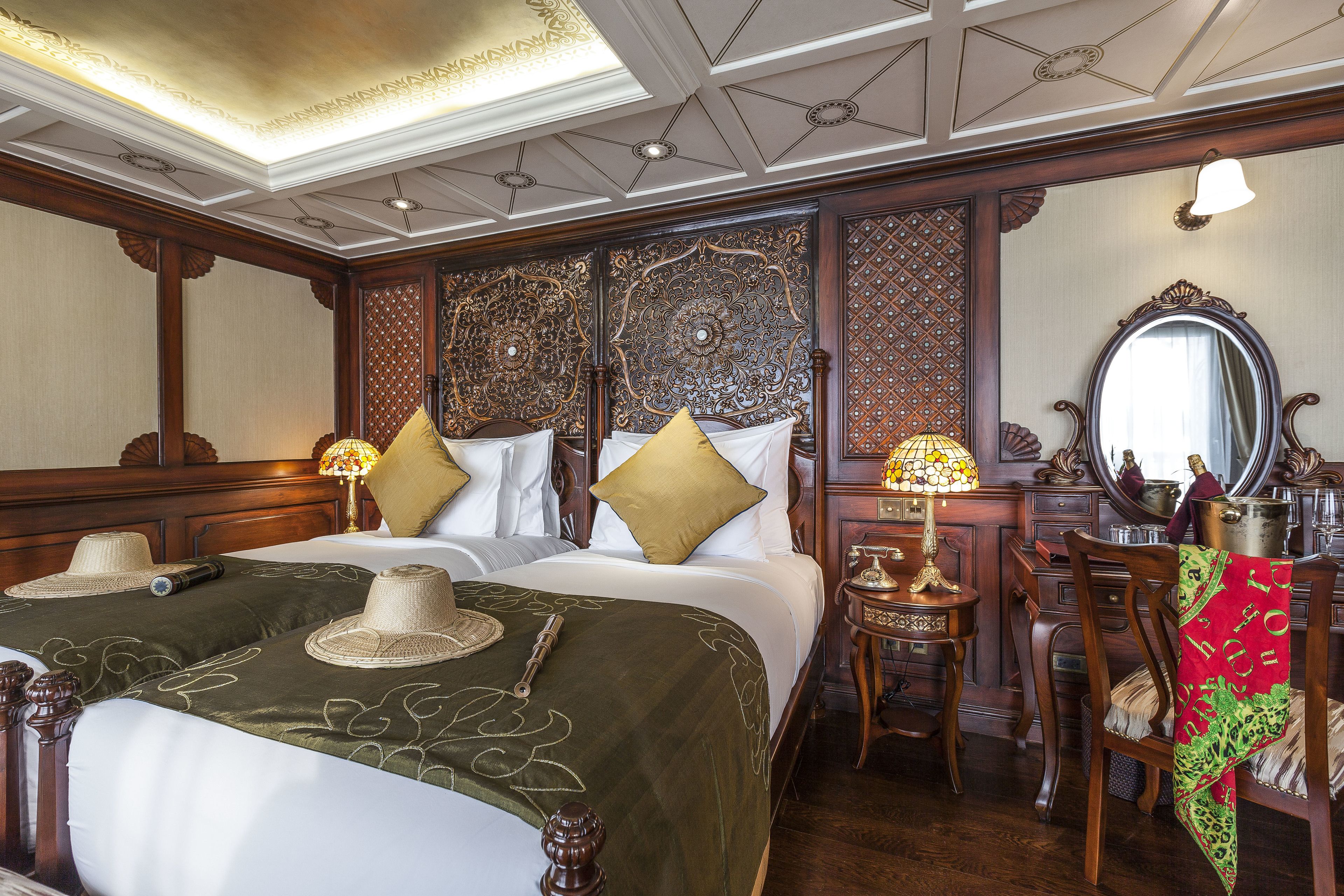 Quarto tradicional com uma cama grande, duas mesas de cabeceira, uma cadeira de madeira e um espelho.