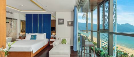 Quarto de hotel moderno com uma cama grande, um sofá e uma varanda com vista para a praia.