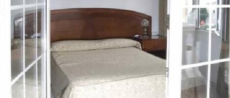 Quarto com cabeceira de madeira, cama com colcha bege, mesa de cabeceira e um quadro na parede.