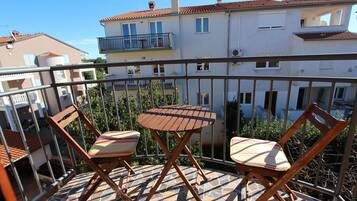 Varanda com duas cadeiras de madeira e uma mesa redonda pequena, com vista para uma área residencial com edifícios e céu claro.