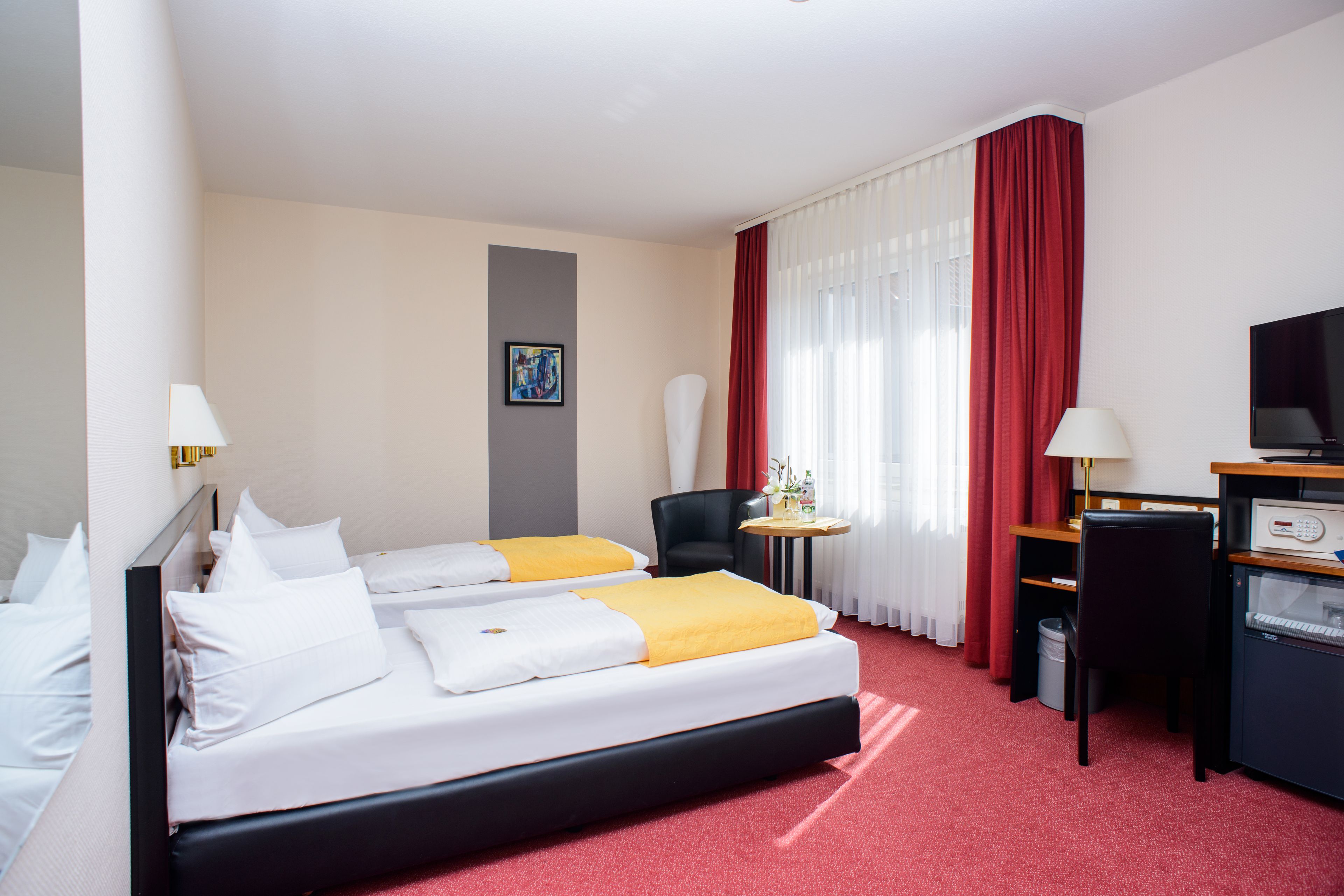 Quarto de hotel com duas camas, uma escrivaninha, uma cadeira, uma televisão e uma mesinha de cabeceira com abajur.